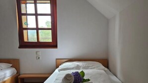Quarto pequeno com cama de solteiro, teto inclinado, janela e um banco de madeira.