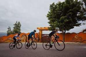 Três ciclistas numa estrada, com um mural e uma árvore ao fundo.