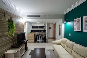Uma sala de estar moderna com um sofá, uma televisão e uma cozinha ao fundo.