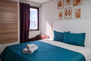Quarto de hotel com cama, janela com cortinas e arte nas paredes.