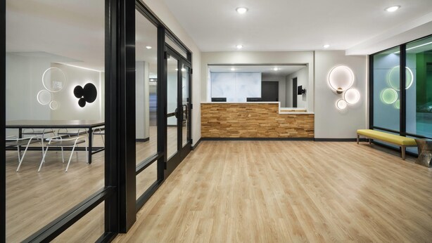 Espaço de escritório moderno com paredes de vidro, balcão de recepção e piso de madeira.