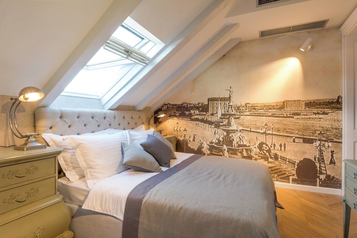 Quarto com claraboia, cama com cabeceira, mesa de cabeceira e cómoda.