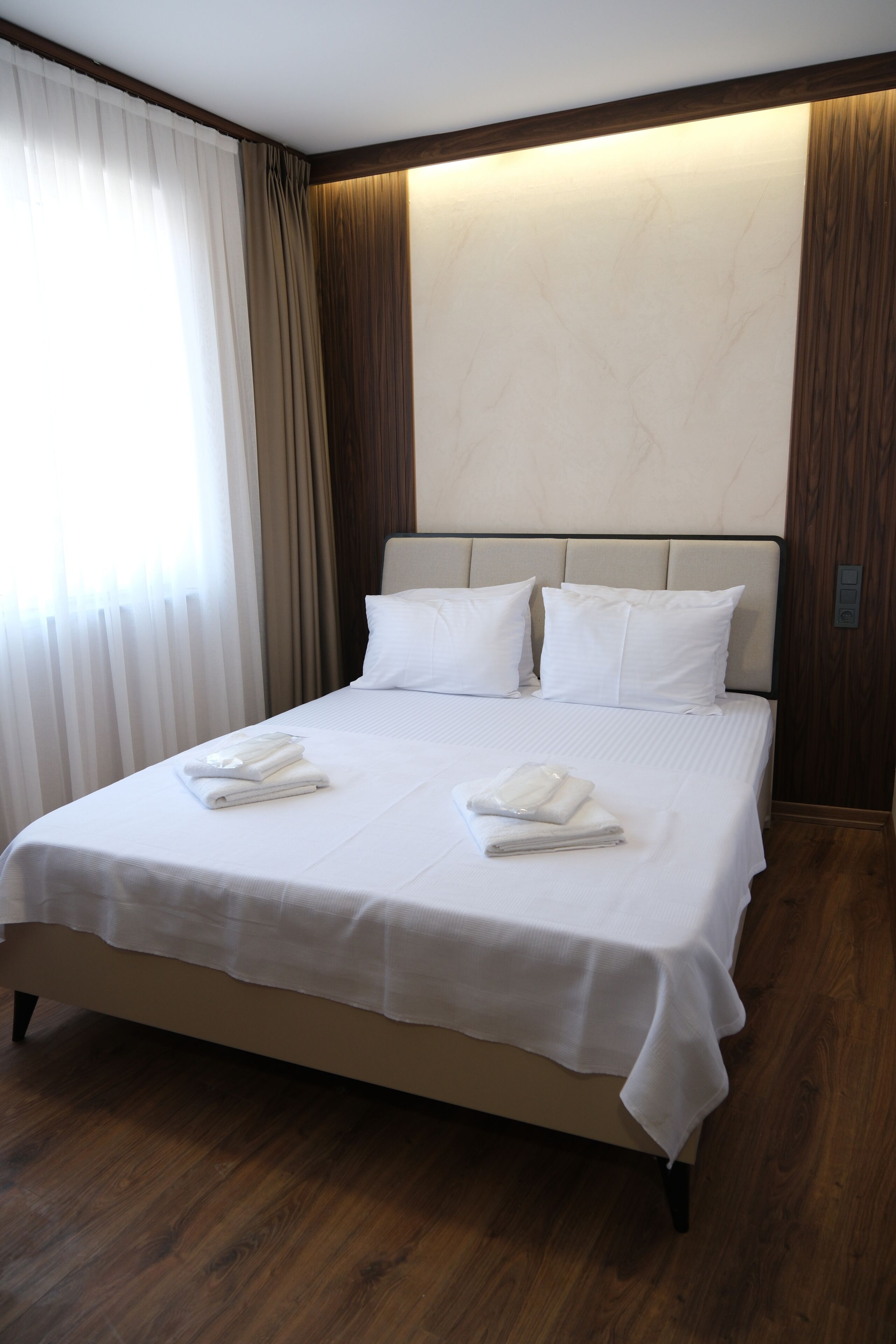 Cama bem arrumada com lençóis e toalhas brancos, cabeceira de madeira e piso de madeira.