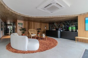 Uma área de recepção moderna com teto curvo, balcão de atendimento, sofá branco, banco de madeira e tapete estampado.