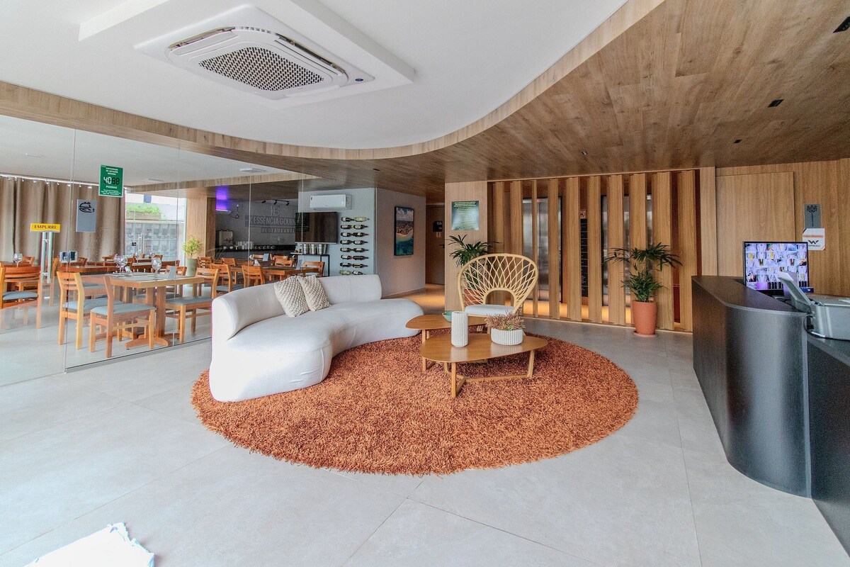 Um hall de hotel moderno com teto de madeira curvo, um sofá branco, uma mesa de centro redonda e um balcão de recepção.