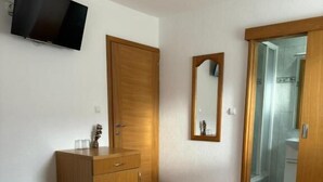 Quarto de hotel com cama, guarda-roupa de madeira, televisão, espelho e porta do banheiro.