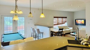 Uma sala de estar moderna com mesa de bilhar, espaço de jantar e cozinha com pia.