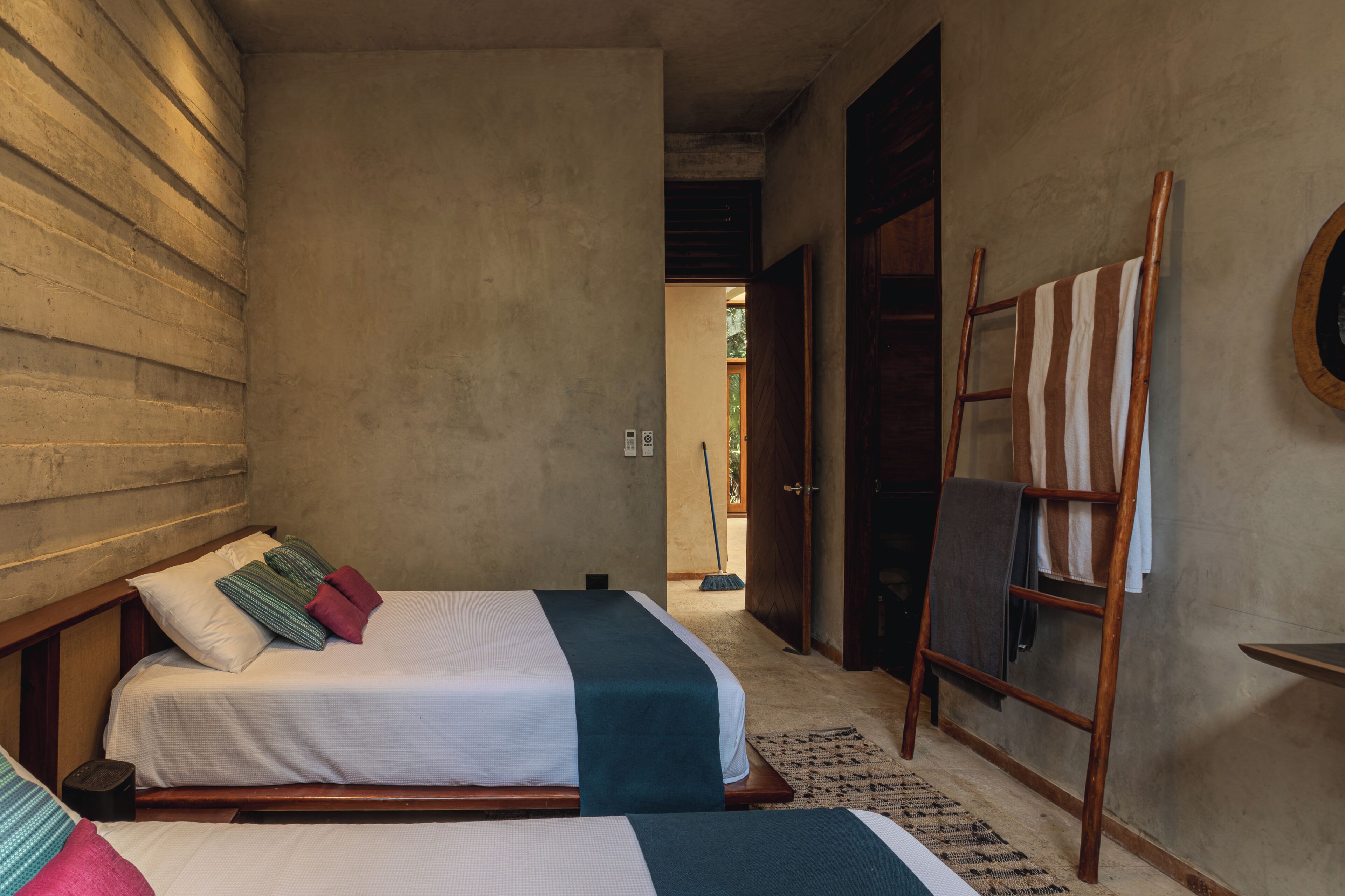 Quarto com duas camas, uma escada de madeira e uma porta que dá para outro cômodo.