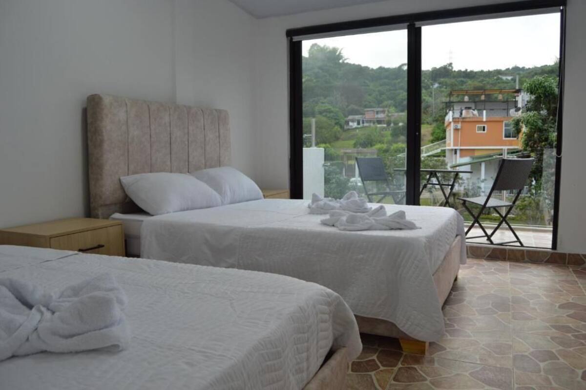 Quarto de hotel com duas camas, uma janela grande e uma varanda com vista para a região.