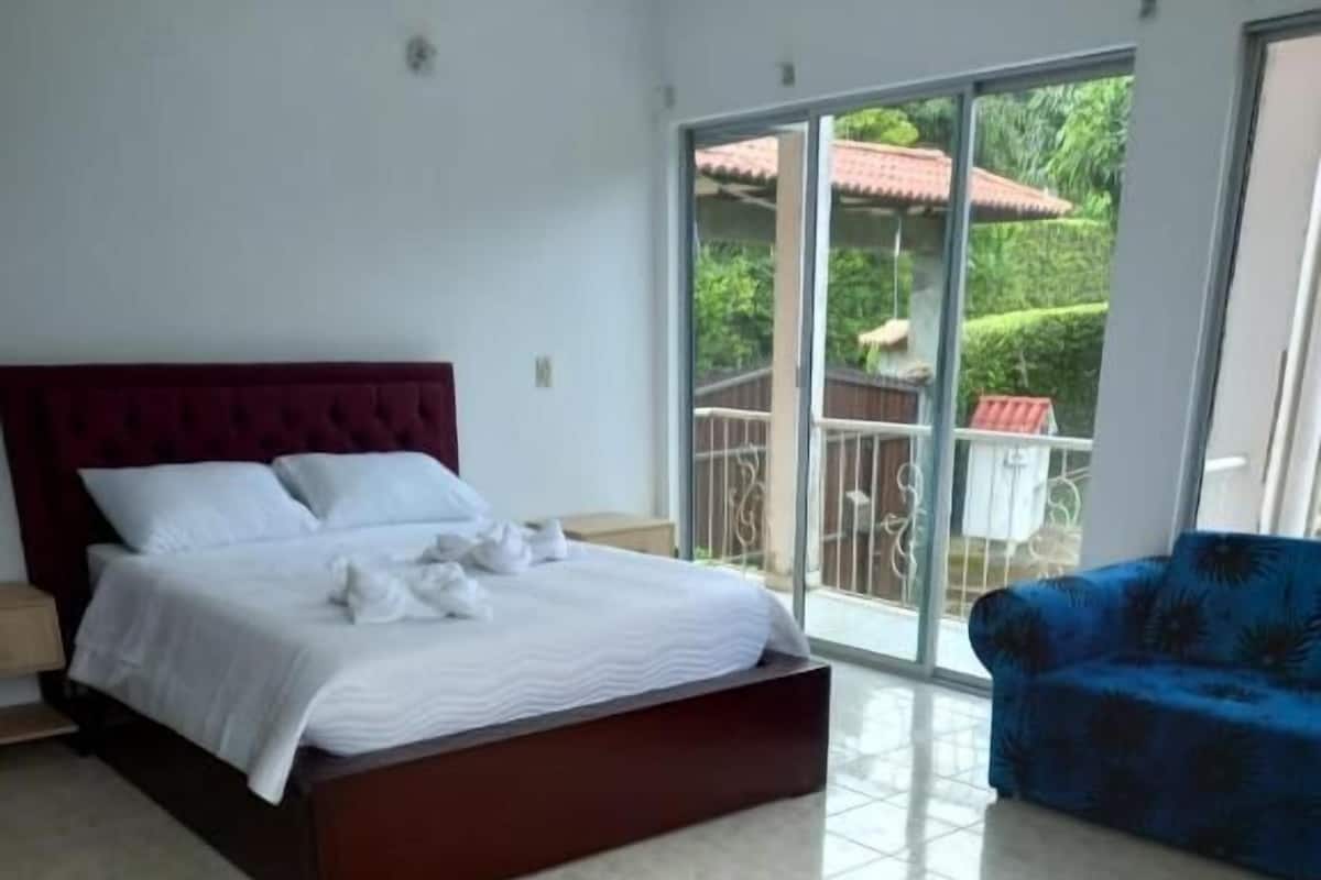 Quarto com cama, sofá azul e varanda com vista.