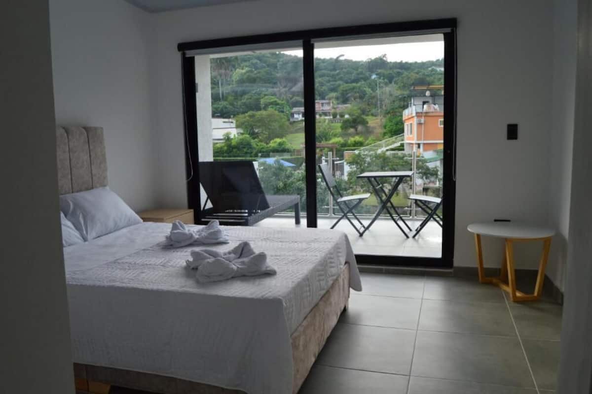 Quarto com cama, mesinha e varanda com cadeira e mesa.