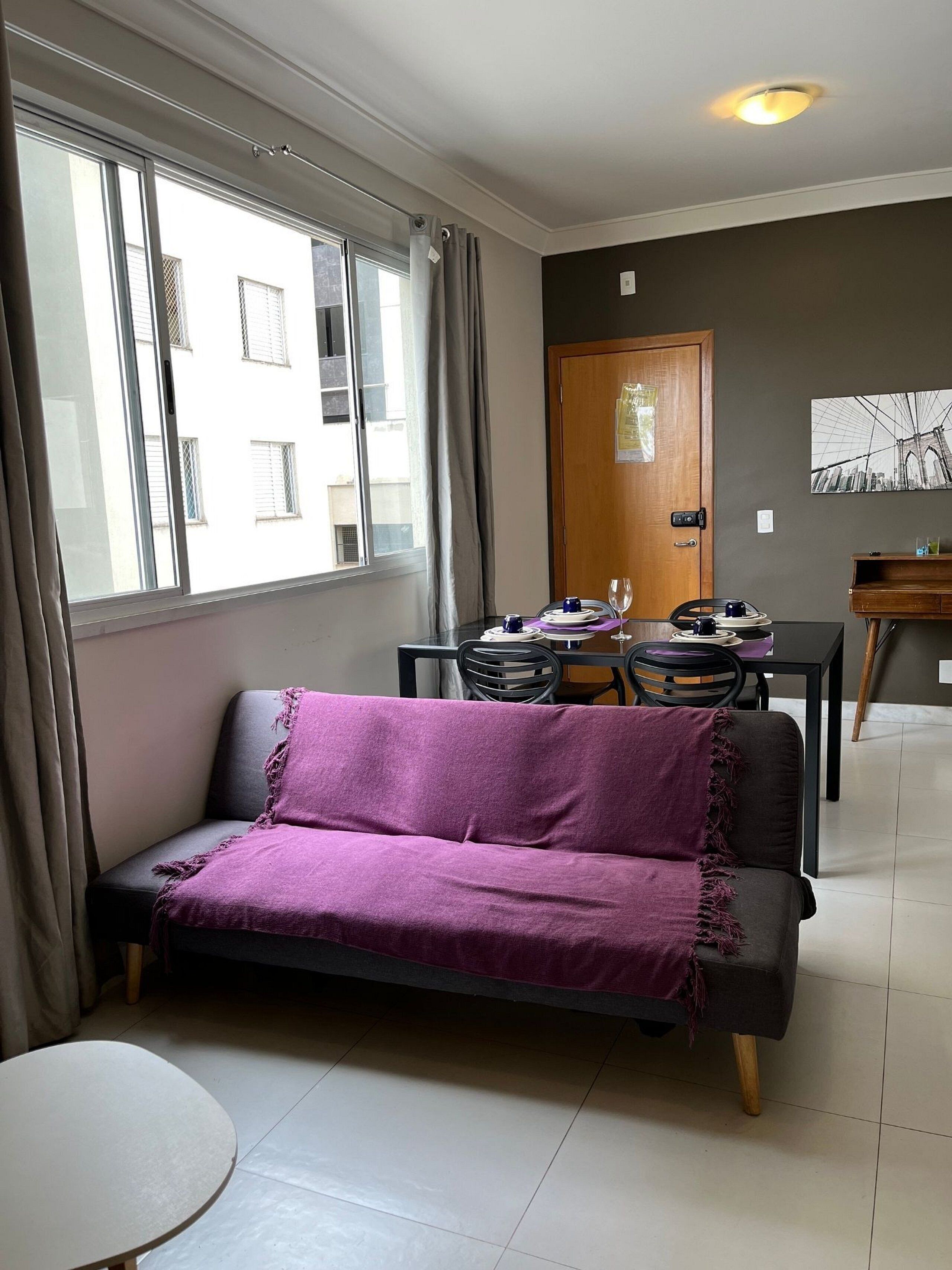 Sala de estar com sofá, mesa de jantar, cadeiras, uma mesinha redonda, uma porta e uma janela.