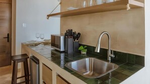 Cozinha com pia de aço inoxidável, prateleiras de madeira, micro-ondas e banquetas.