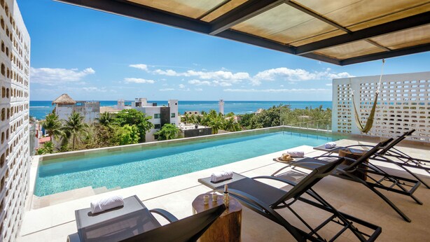 Área de piscina com espreguiçadeiras, piscina e vista para o mar.