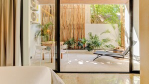 Quarto moderno com cama, área de refeições e vista para espaço externo com plantas e parede de bambu.
