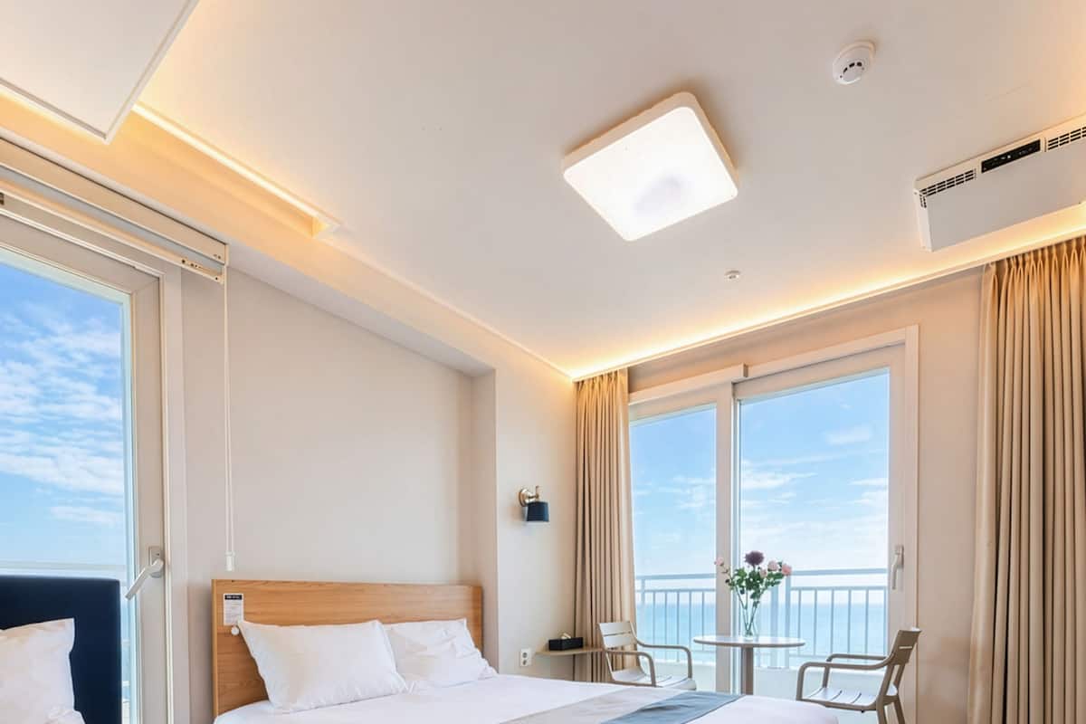 Quarto de hotel com duas camas, uma varanda com mesa e cadeiras, e uma janela grande com vista.