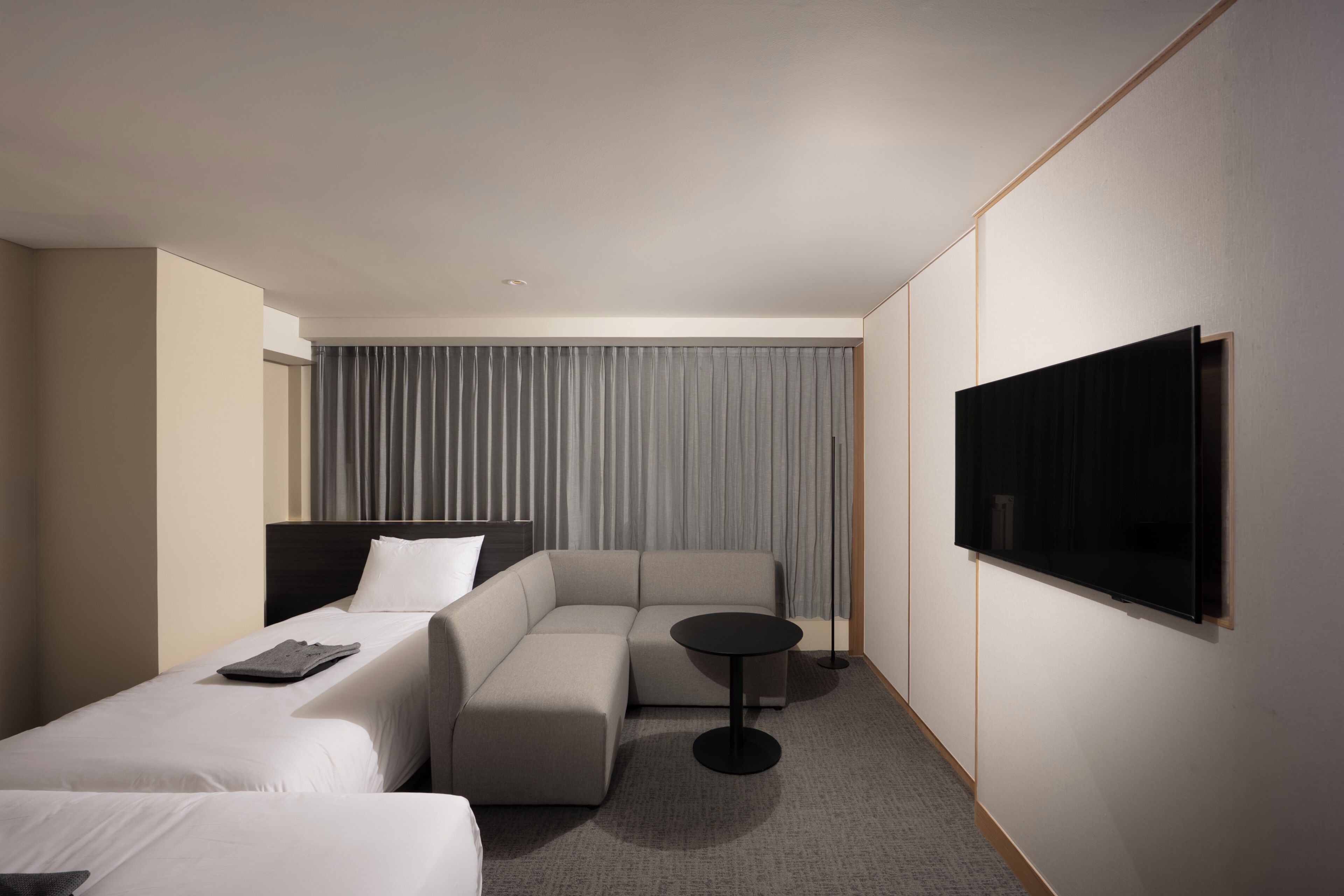 Quarto de hotel com cama, sofá, mesa pequena e televisão.