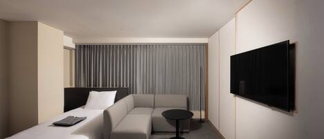 Quarto de hotel com cama, sofá, mesa pequena e televisão.