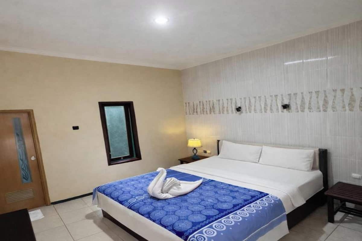 Quarto de hotel com uma cama, mesa de cabeceira, abajur, porta e janela.