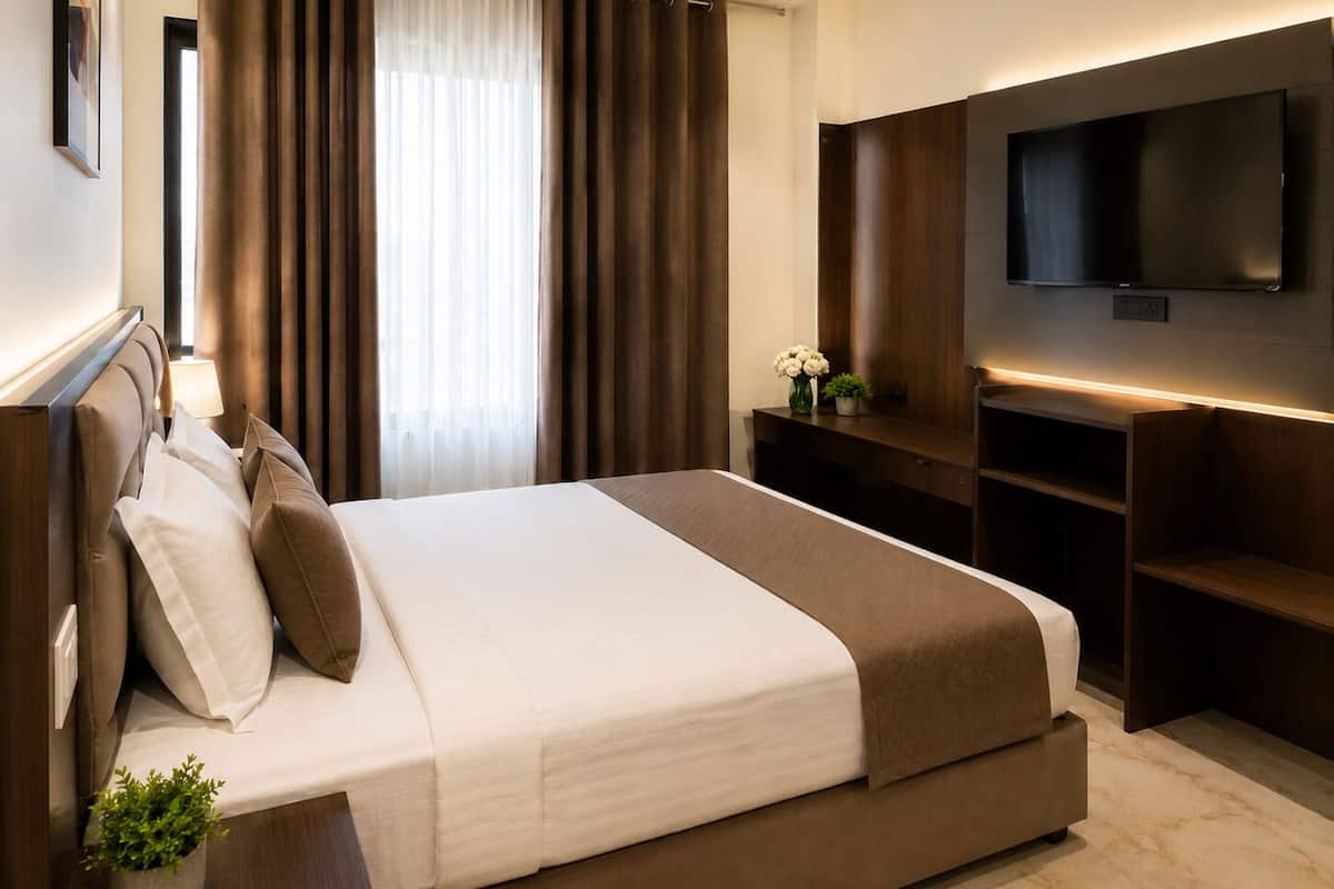 Quarto de hotel moderno com uma cama grande, televisão de tela plana na parede e janela com cortinas.