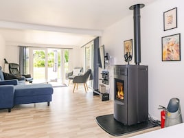Uma sala de estar moderna com uma lareira a lenha, um sofá, uma poltrona e uma salamandra.