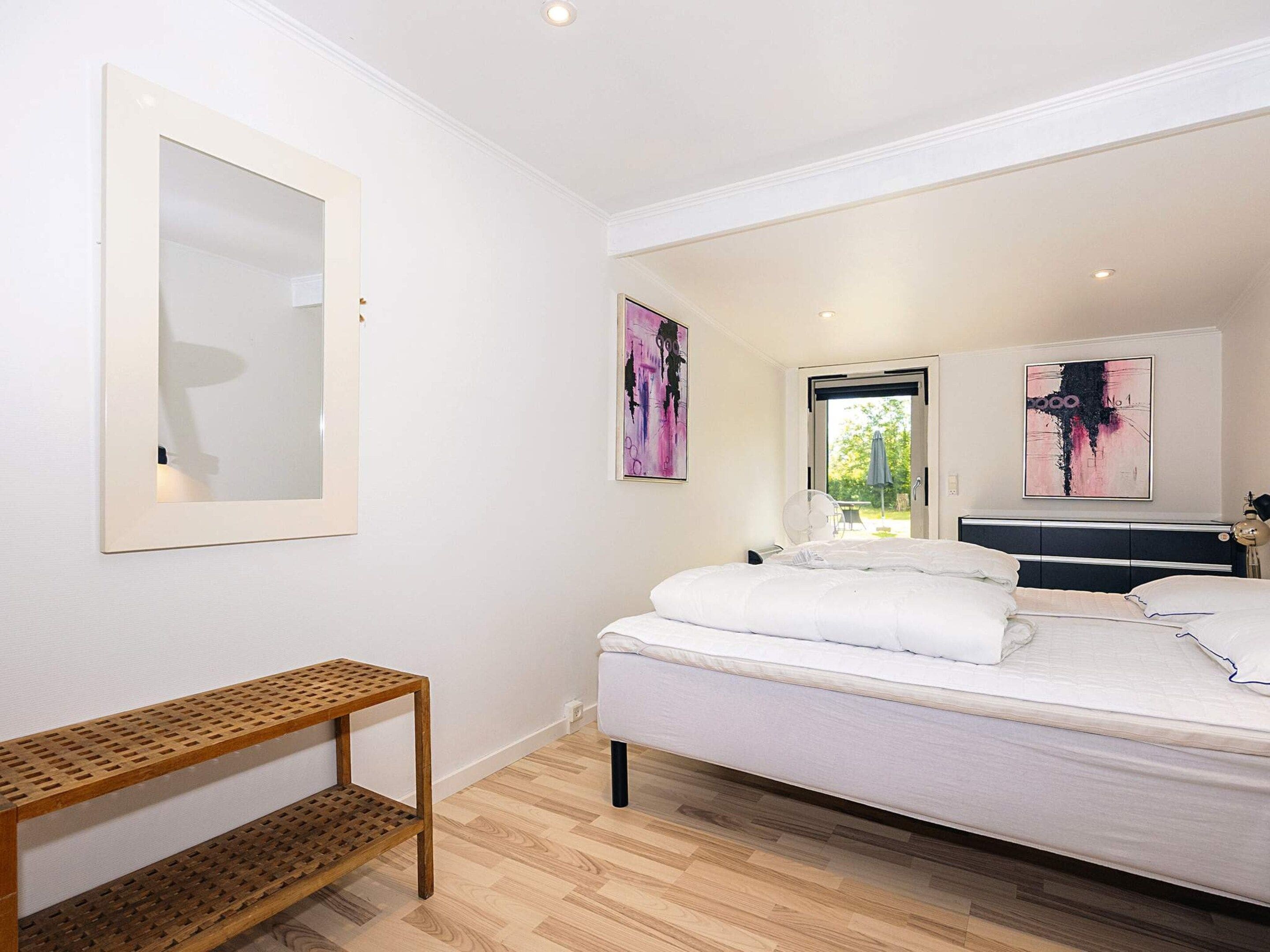 Quarto com cama, um banco de madeira e duas obras de arte na parede.