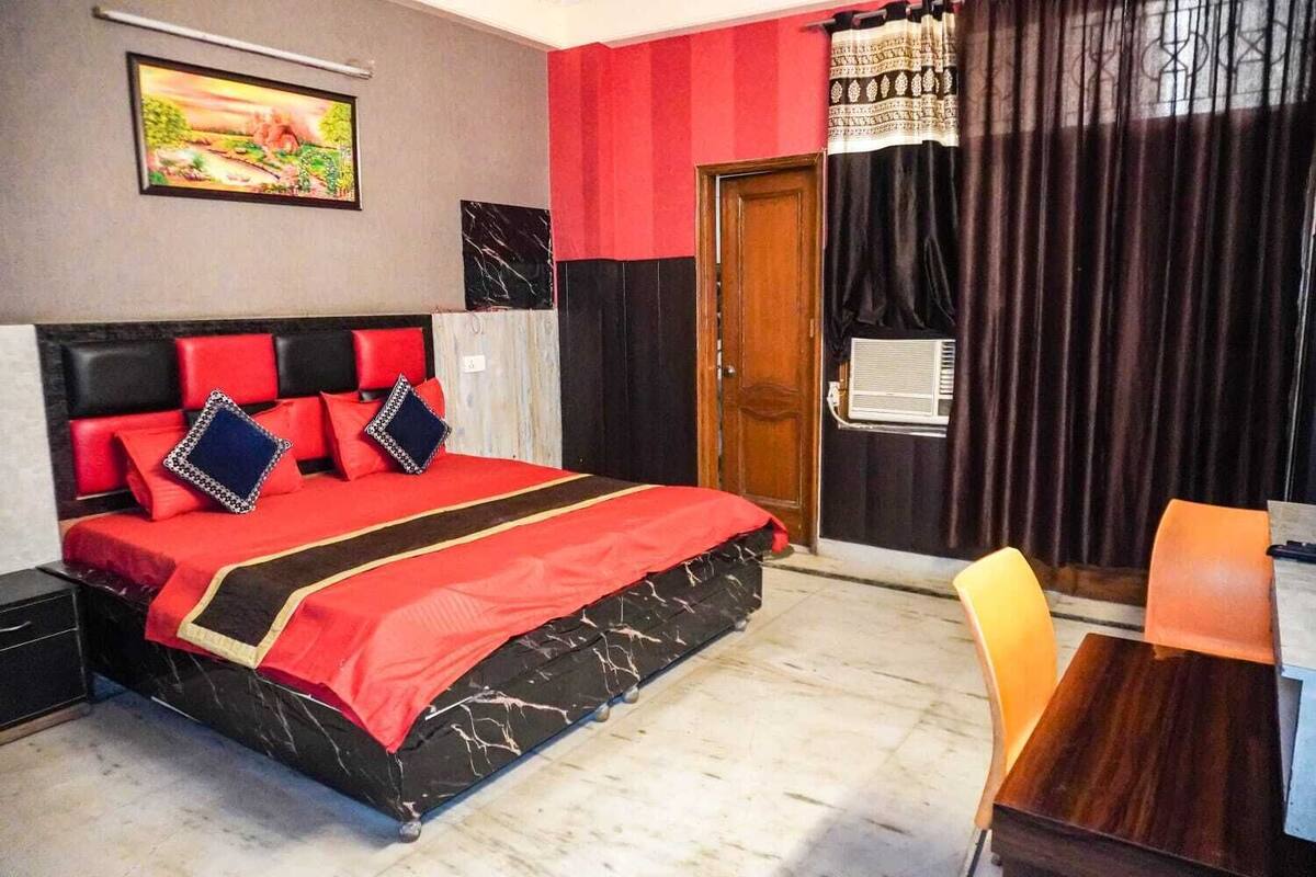 Quarto de hotel com cama, escrivaninha, cadeira, porta e um quadro na parede.