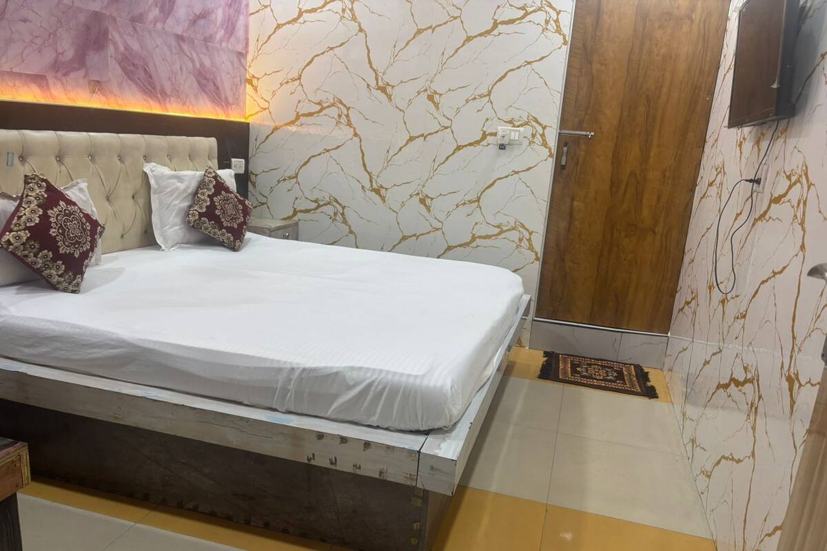 Quarto com cama, guarda-roupa de madeira, paredes com padrão marmorizado e televisão na parede.
