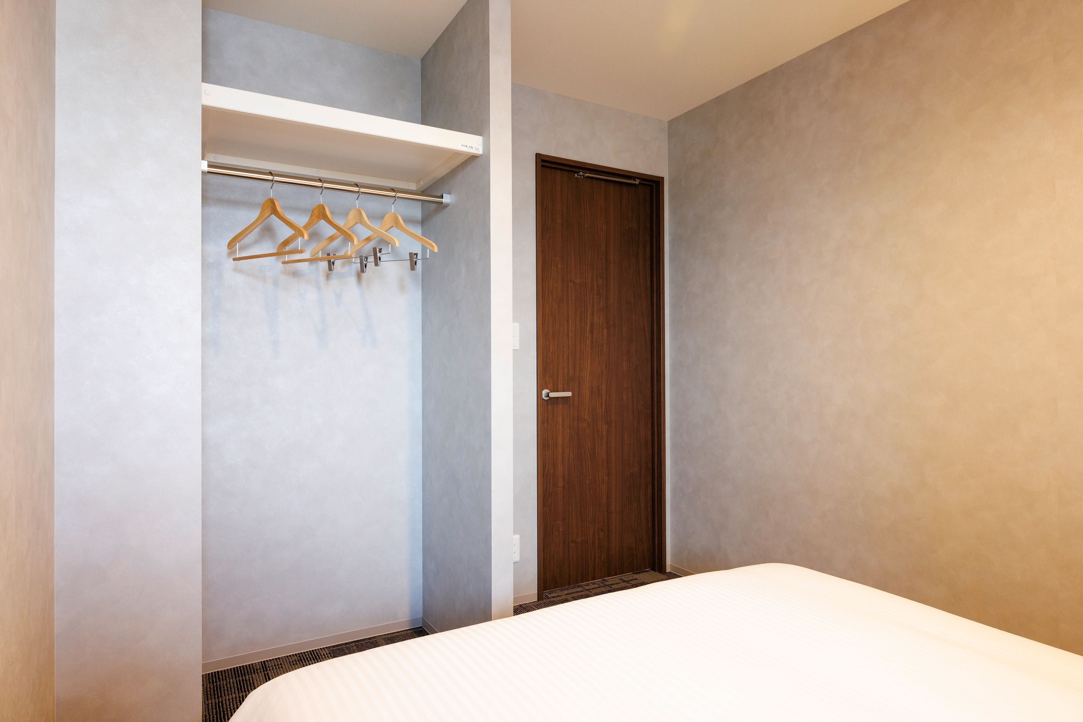 Quarto de hotel com cama, guarda-roupa de madeira e cabideiro com cabides.