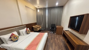 Quarto de hotel com cama, escrivaninha, cadeira, televisão e cortina.