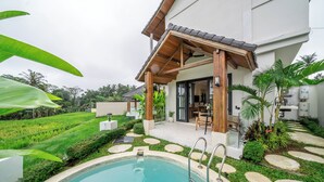 Uma piscina com deck de madeira, varanda coberta e jardim exuberante.