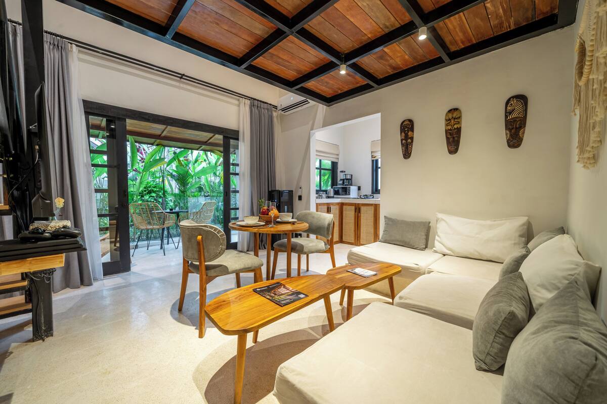 Uma sala moderna com sofá, mesa de centro e cadeiras, área de cozinha e varanda com plantas.
