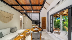 Um interior moderno com sofá, mesa de jantar e cadeiras, escada e vista para o verde através de uma porta de vidro.