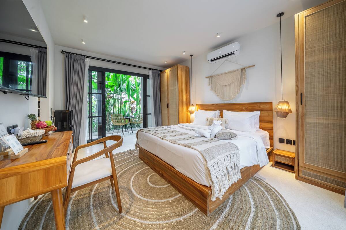 Quarto com cama, mesa de cabeceira e vista para o verde lá fora.