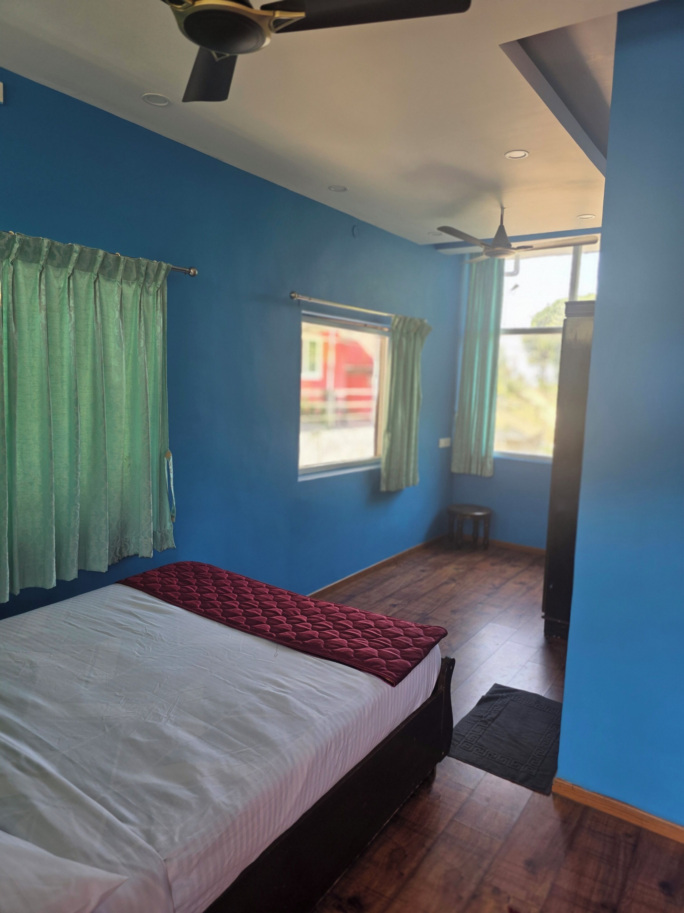 Quarto com cama, ventoinha no teto, janela com cortinas e vista para o exterior.