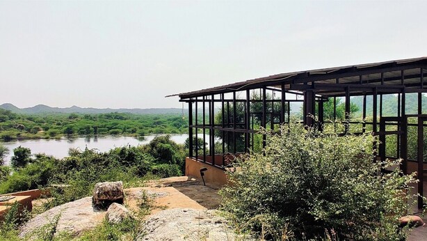 Uma estrutura envidraçada com vista para um lago e colinas.