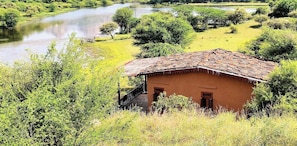 Um edifício rústico com telhado de telhas, rodeado por vegetação exuberante e um rio ao fundo.