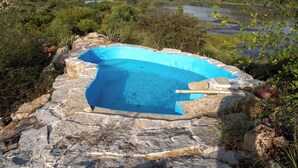 Piscina natural rodeada por terreno rochoso e vegetação.