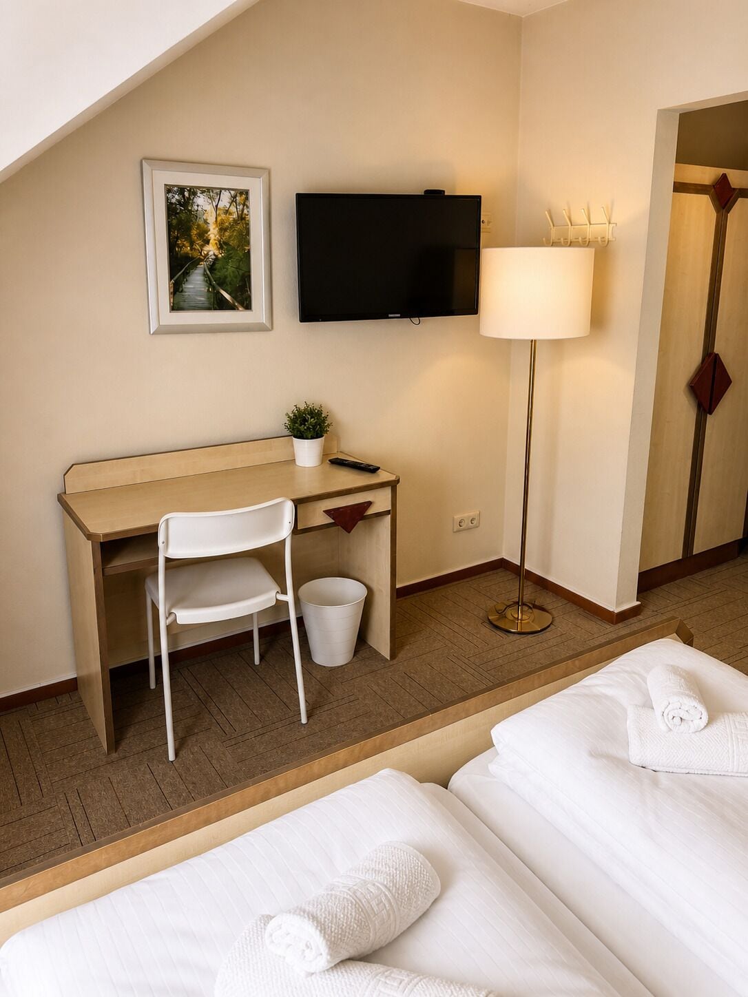 Quarto de hotel com escrivaninha, cadeira, televisão, luminária e duas camas com toalhas.