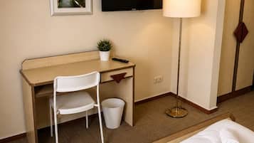 Quarto de hotel com escrivaninha, cadeira, televisão, luminária e duas camas com toalhas.