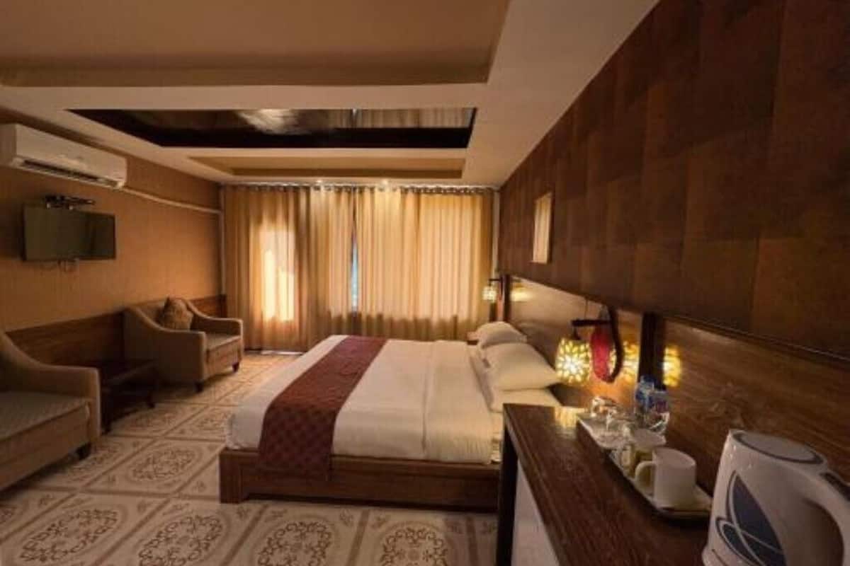 Quarto de hotel com cama, duas poltronas, televisão, máquina de café e janela com cortinas.