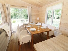 Um quarto com painéis de madeira, mesa de jantar posta para seis pessoas, cadeiras brancas, um sofá e janelas amplas.