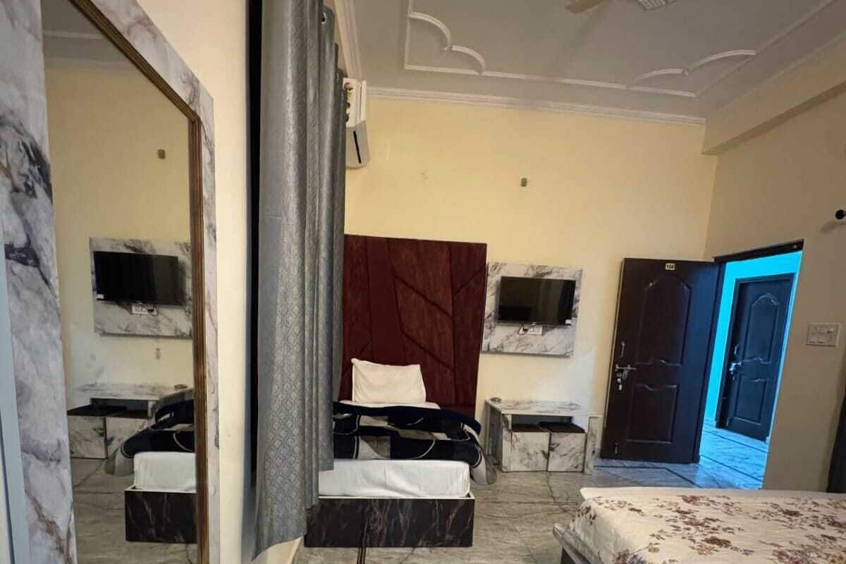 Quarto de hotel com uma cama, televisão, guarda-roupa, espelho e ventoinha no teto.