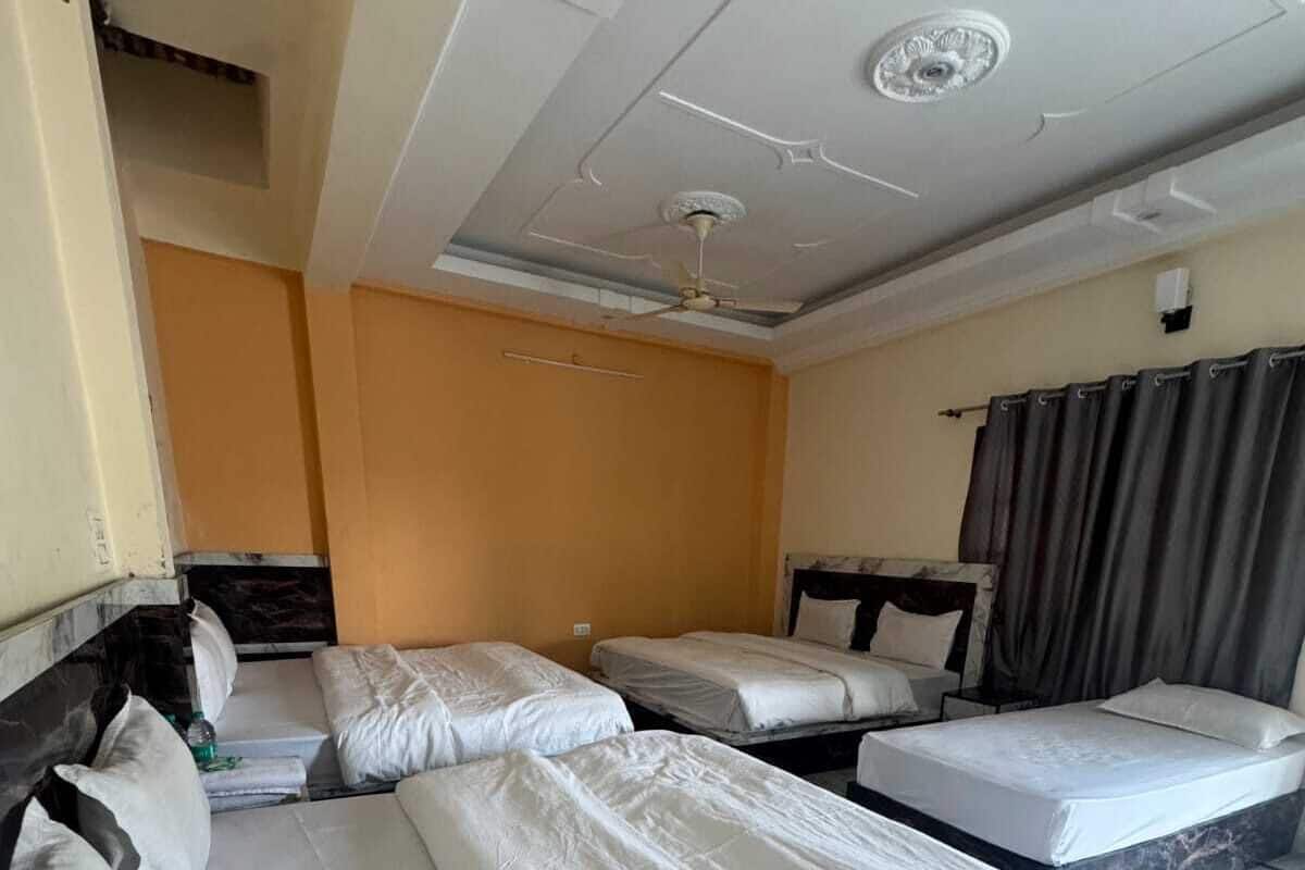 Quarto de hotel com três camas, um ventilador de teto e cabeceira de mármore.