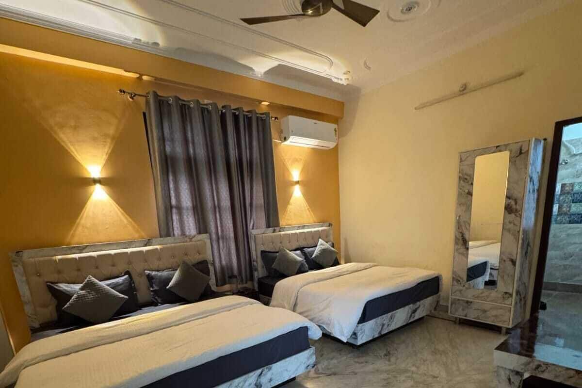 Quarto de hotel com duas camas, um ventilador de teto, ar-condicionado fixado na parede e piso com padrão marmorizado.
