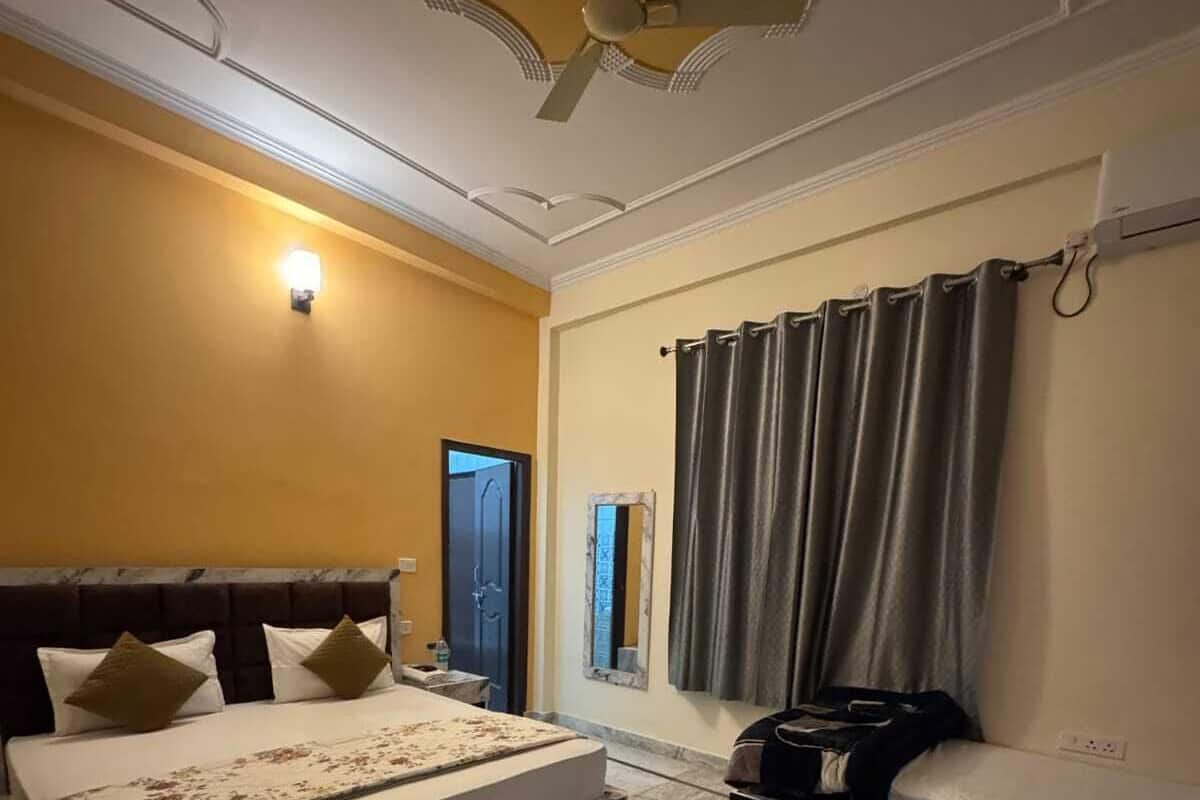 Quarto com cama, mesa de cabeceira, guarda-roupa, ventilador de teto e janela com cortinas.