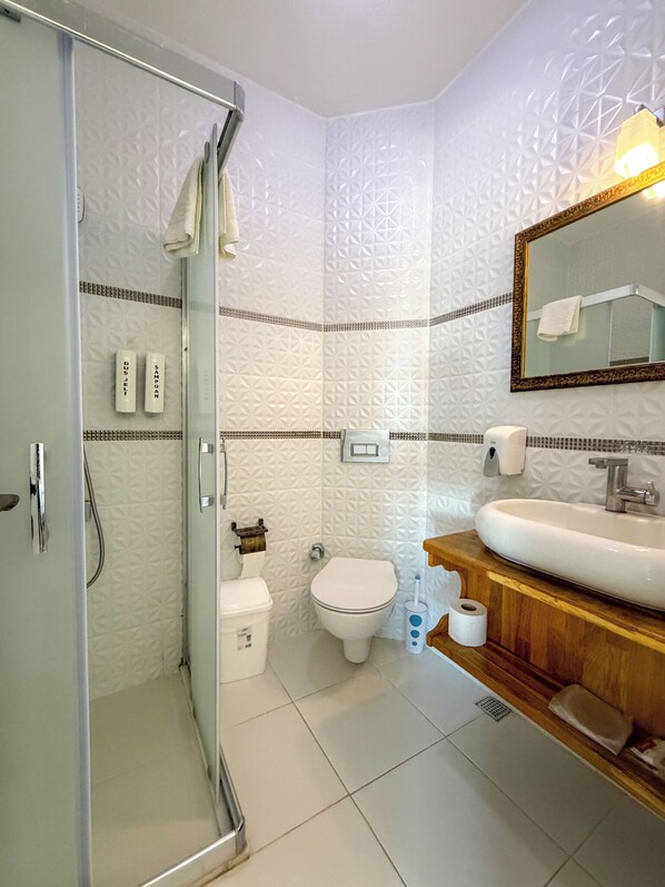 Casa de banho com cabine de chuveiro em vidro, sanita, lavatório com espelho e azulejos estampados.