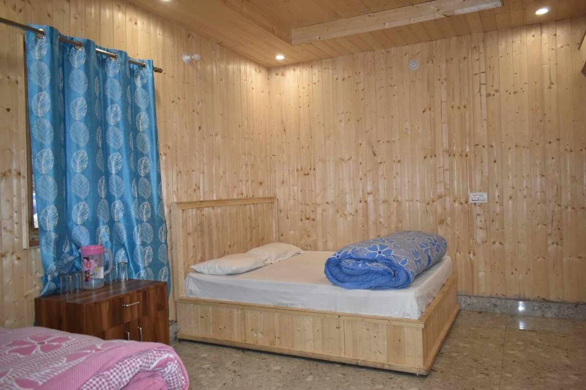 Quarto com painéis de madeira, uma cama, uma mesinha e uma janela com cortinas azuis.