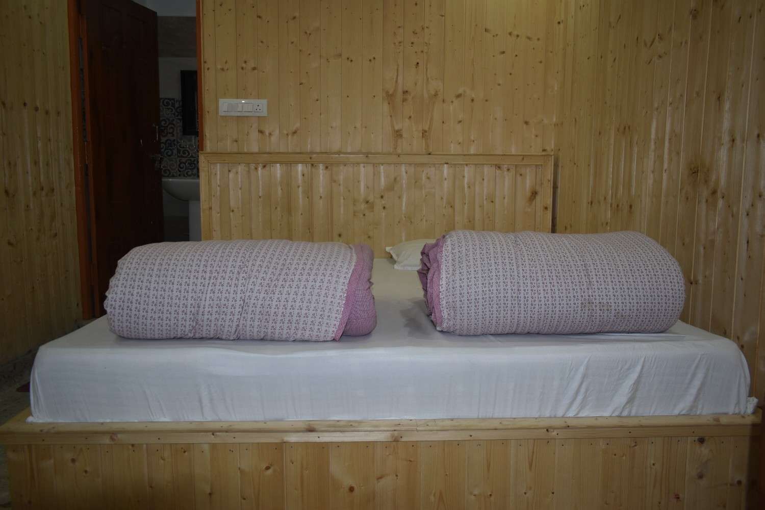 Uma cama beliche de madeira com dois travesseiros, um colchão branco e um encosto de madeira.