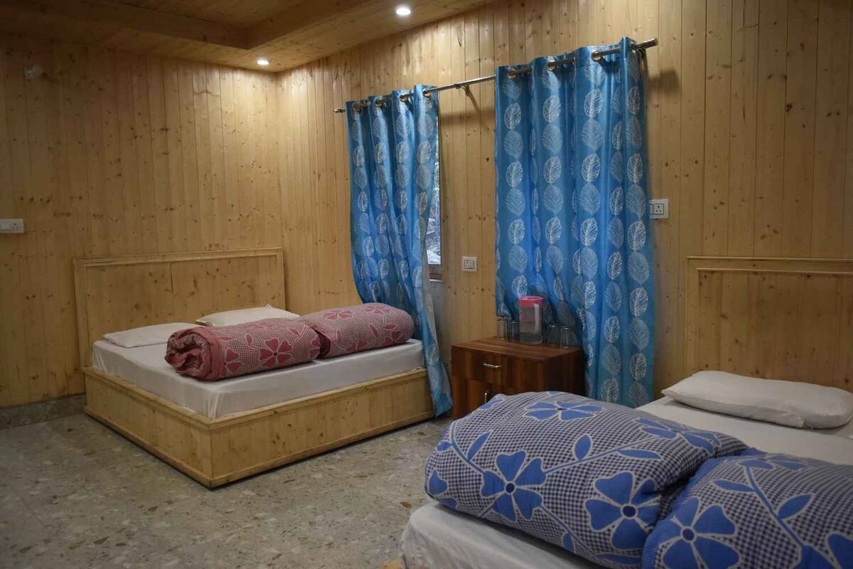 Quarto de madeira com duas camas, uma com manta rosa estampada e outra com almofadas azuis estampadas.